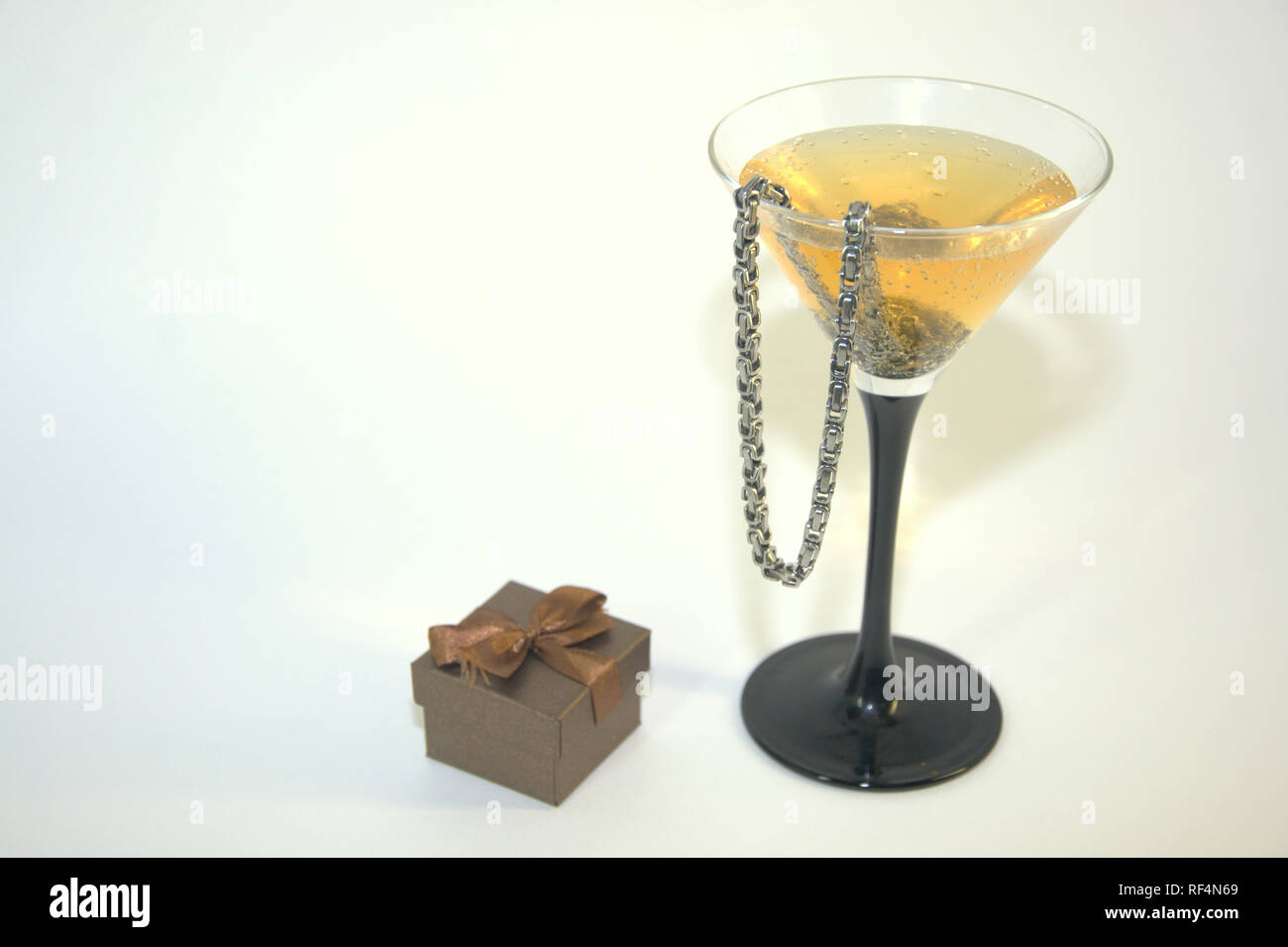 A glass of champagne with a chain inside and a small gift box. Close-up ...