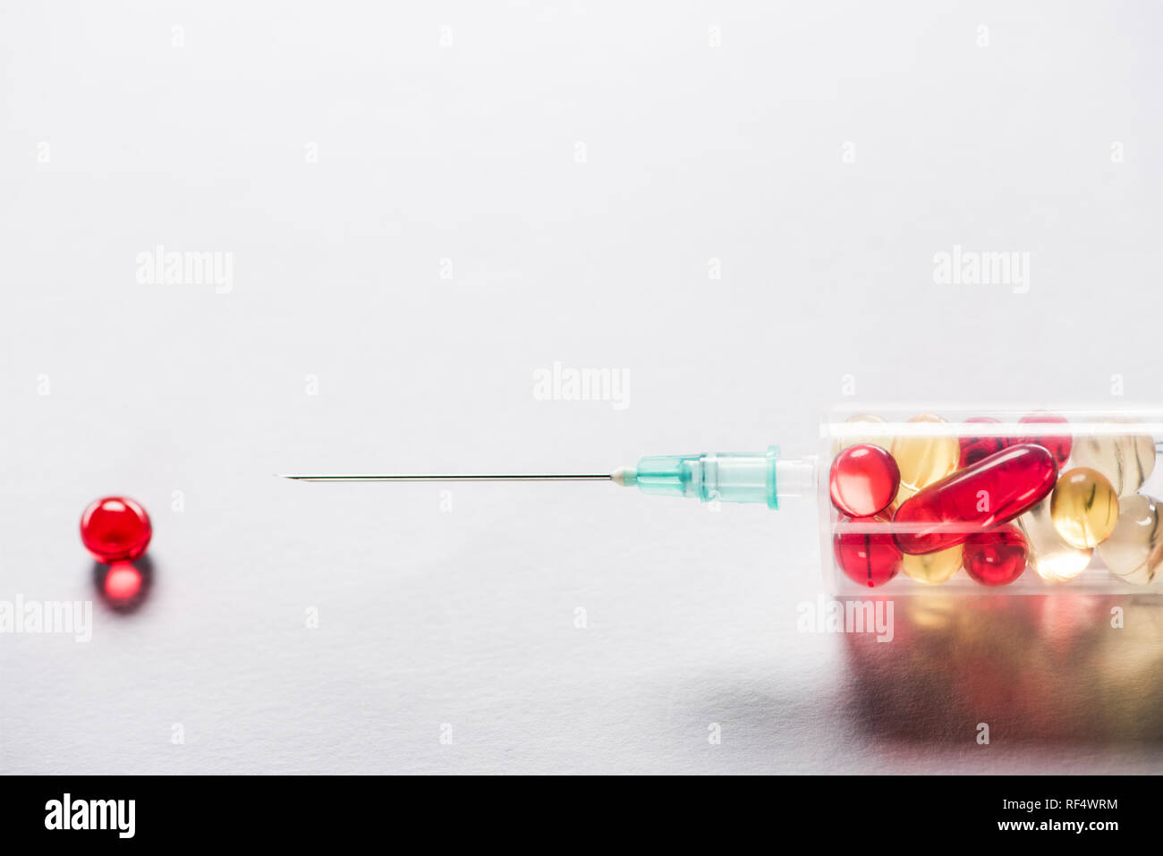 close up of syringe with medication near red round pill on grey ...