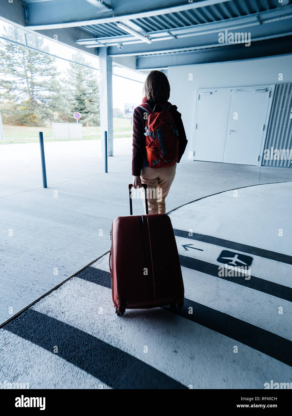 Woman exiting airport parking carrying big red luggage walking to the ...