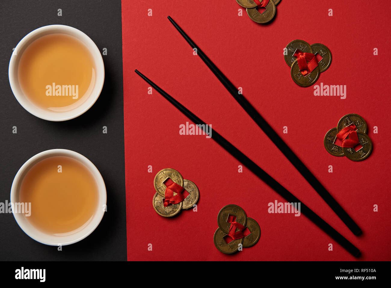 top view of tea cups, feng shui coins and chopsticks on red and black ...