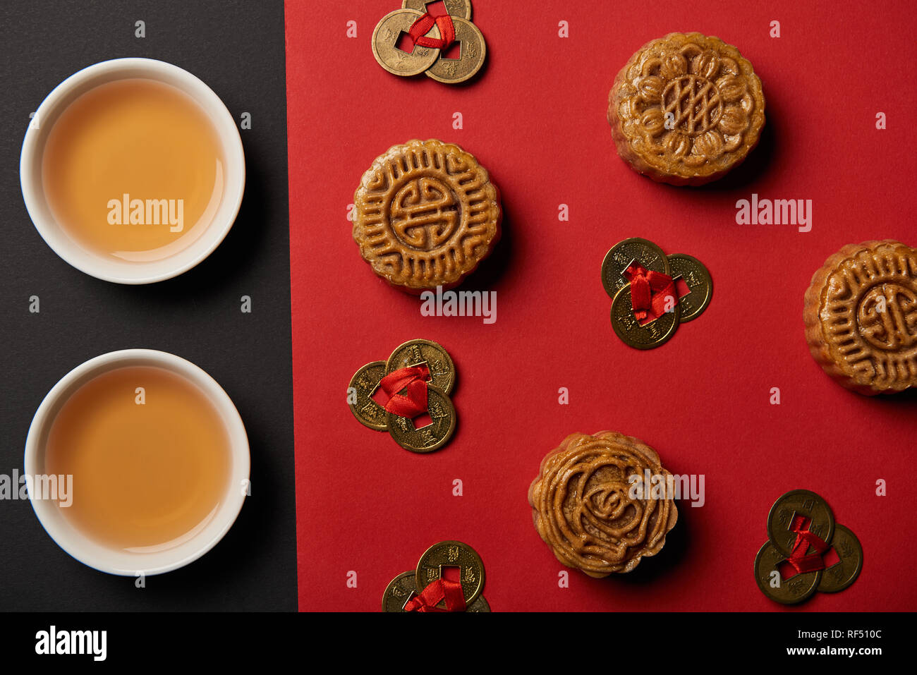 top view of mooncakes, feng shui coins and cups with tea on red and ...