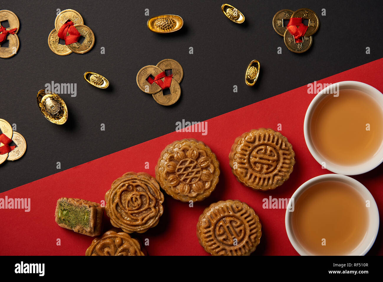 top view of mooncakes, feng shui coins and cups with tea on red and ...