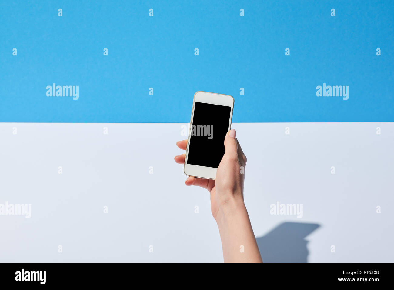 cropped view of woman using smartphone with blank screen on white desk ...