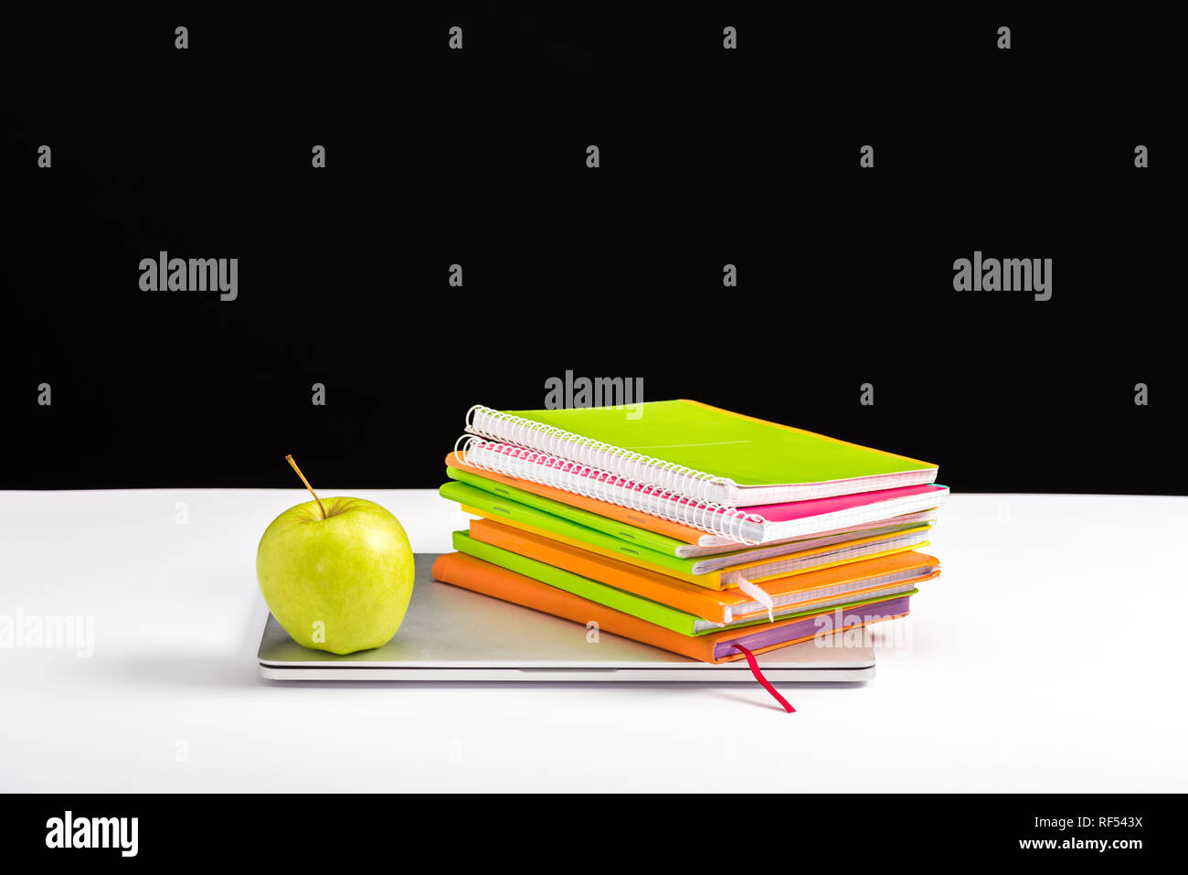 colorful notebooks, apple and laptop on desk isolated on black with ...