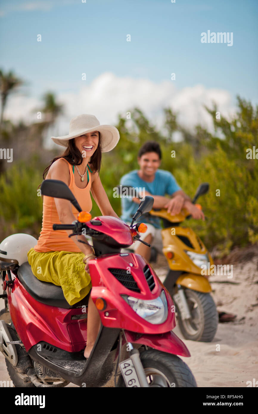 Smiling young couple having fun riding moped scooters along a tropical ...