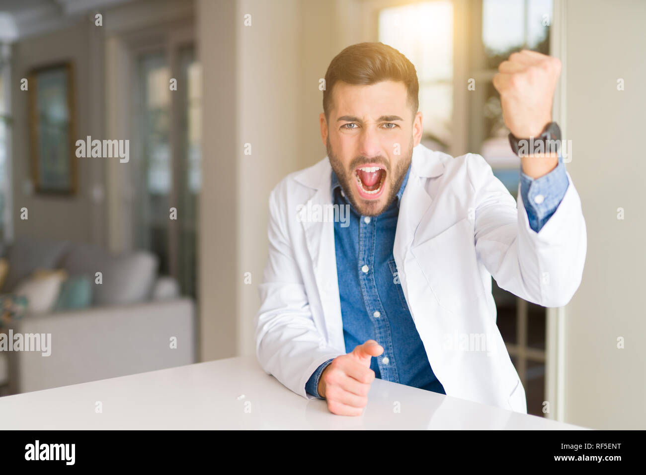 Young handsome doctor man at the clinic angry and mad raising fist ...