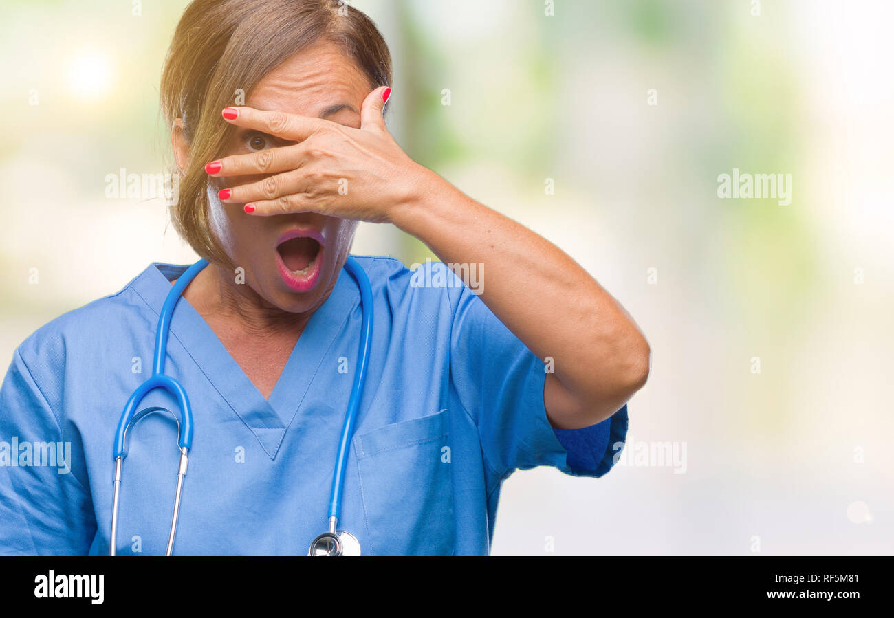 Middle age senior nurse doctor woman over isolated background peeking ...