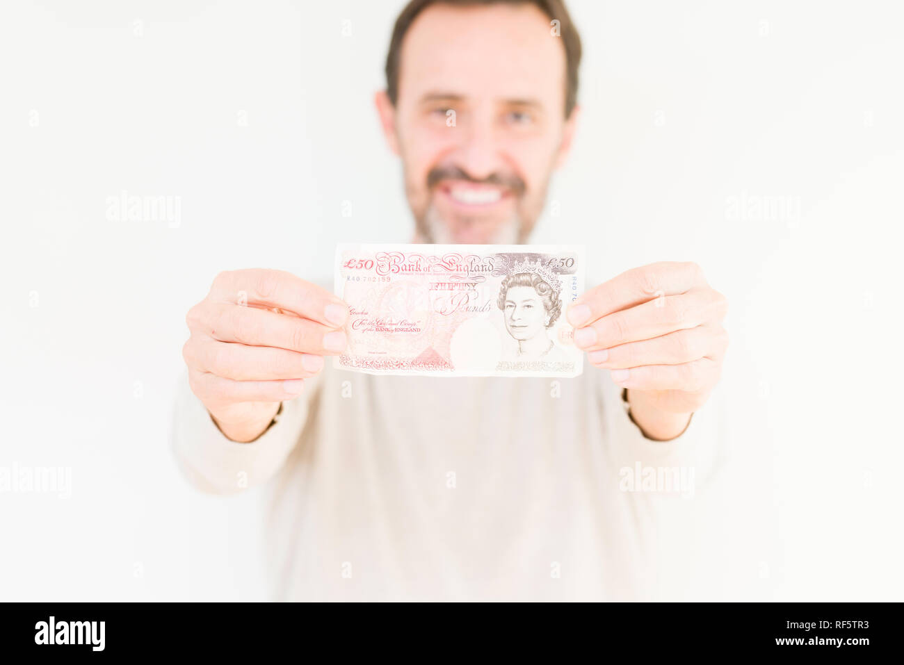 Senior man holding fifty pounds bank note over isolated background with ...