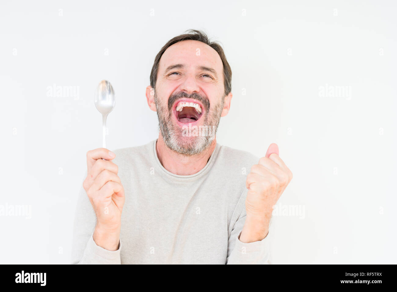 Senior man holding silver spoon over isolated background screaming ...