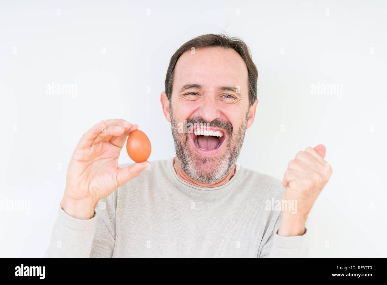 Senior man holding fresh egg over isolated background screaming proud ...