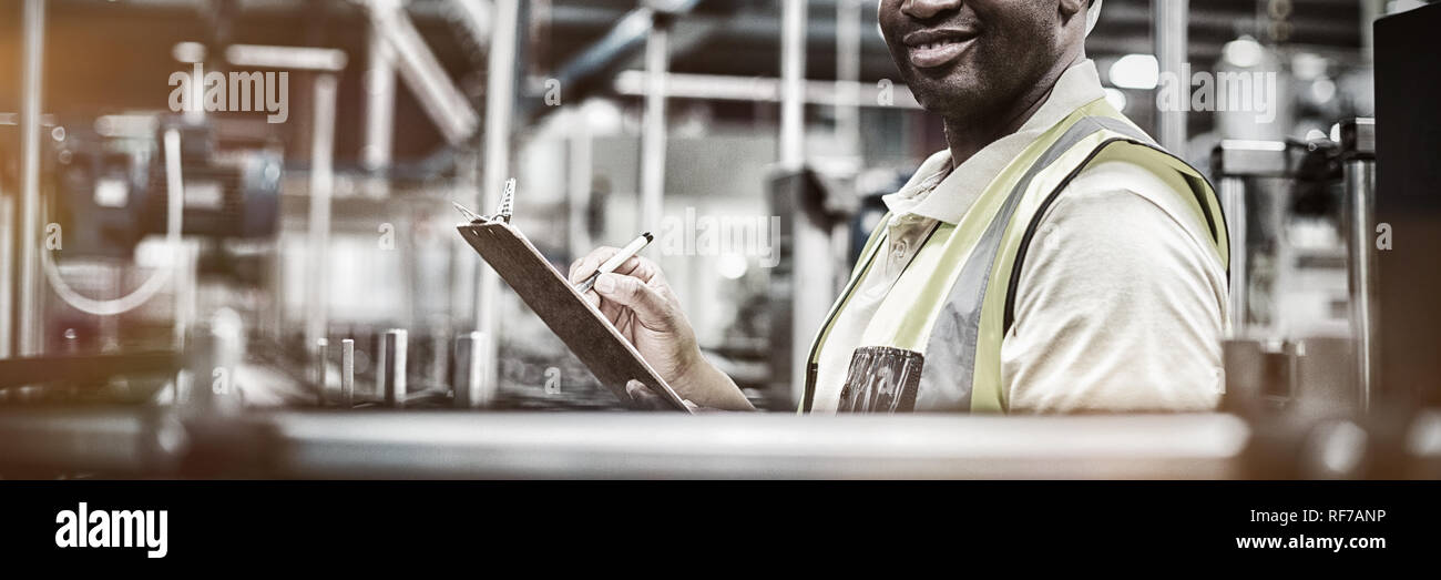 Portrait of smiling factory worker writing on clipboard in factory ...