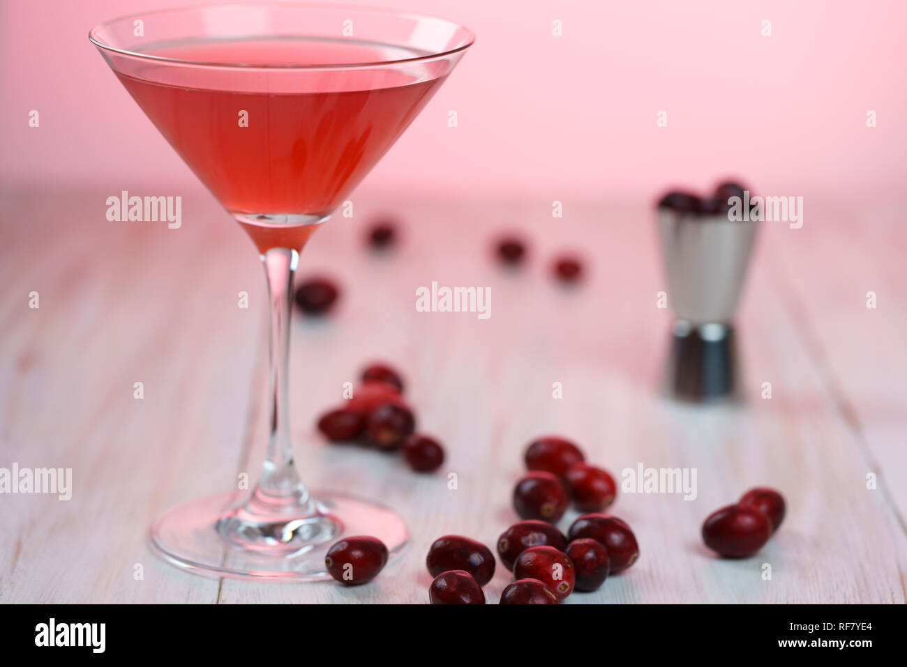 Cosmopolitan cocktail with cranberries, shaker and jigger. White wooden ...