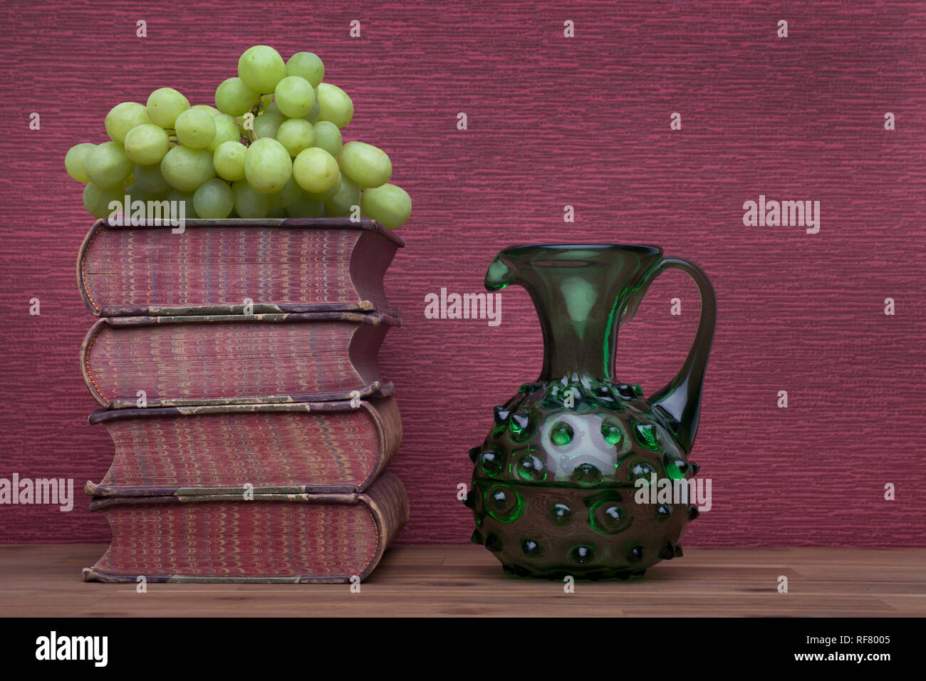 Renaissance, wine carafe, bottle, old books and grapes on the burgundy ...