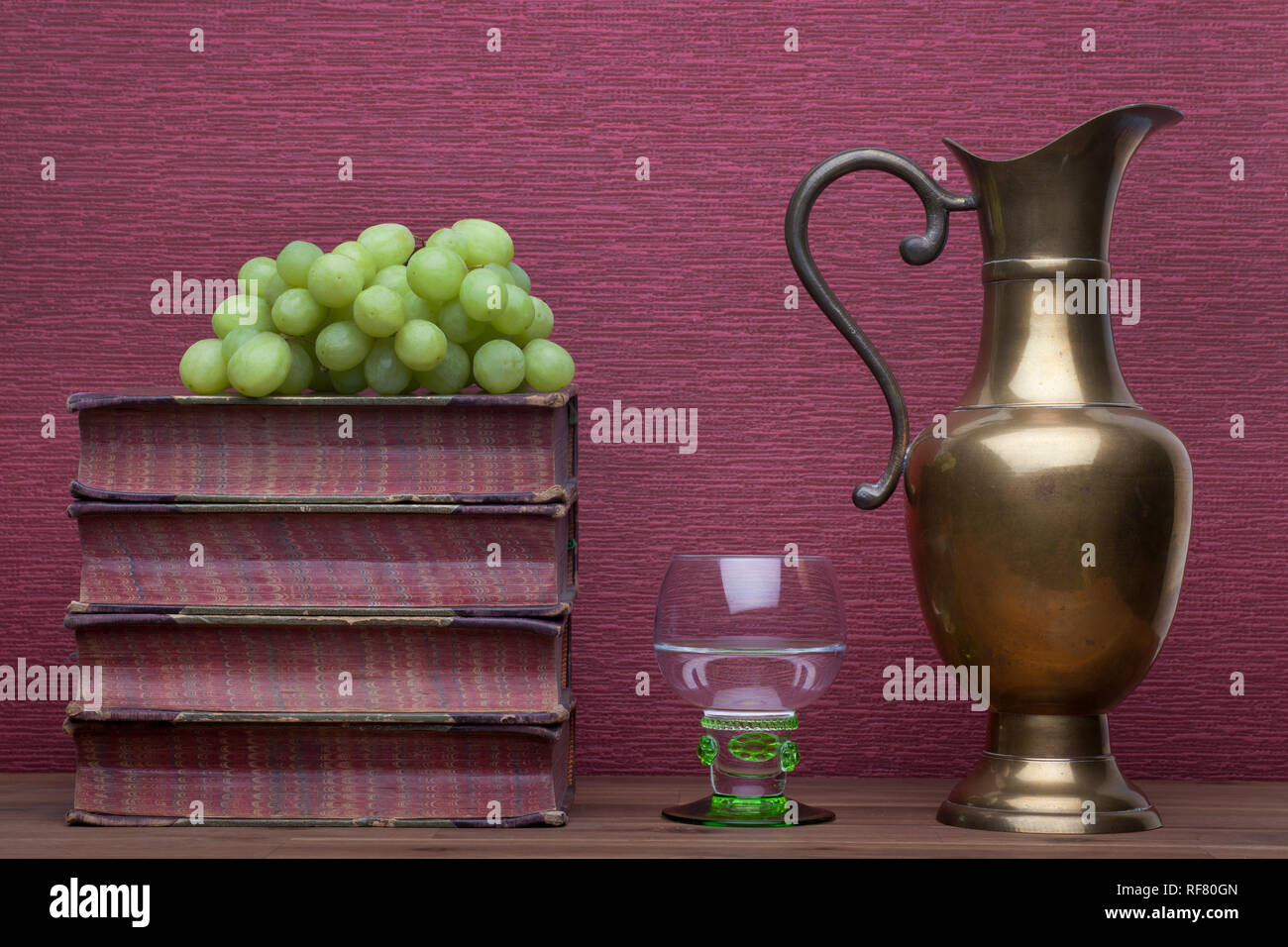Renaissance, rummer wine glass, brass carafe, old books and grapes on ...