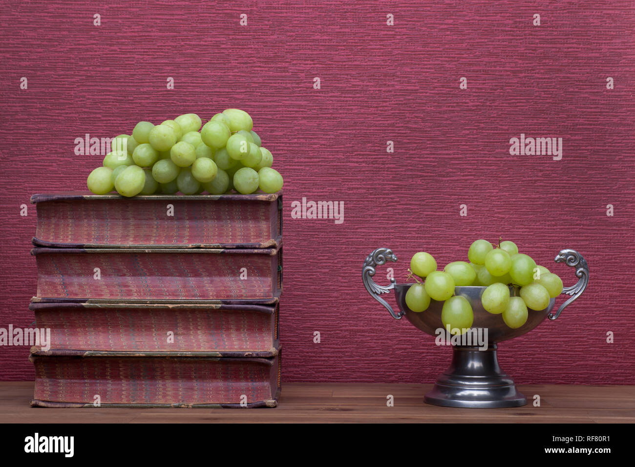 Renaissance, tin cup old books and grapes on the burgundy background ...