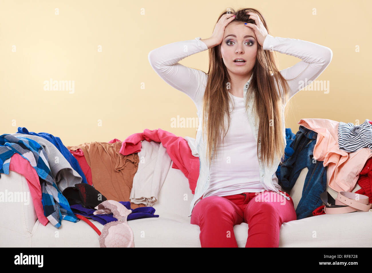 Desperate helpless woman sitting on sofa couch in messy living room with hands on head. Young ...
