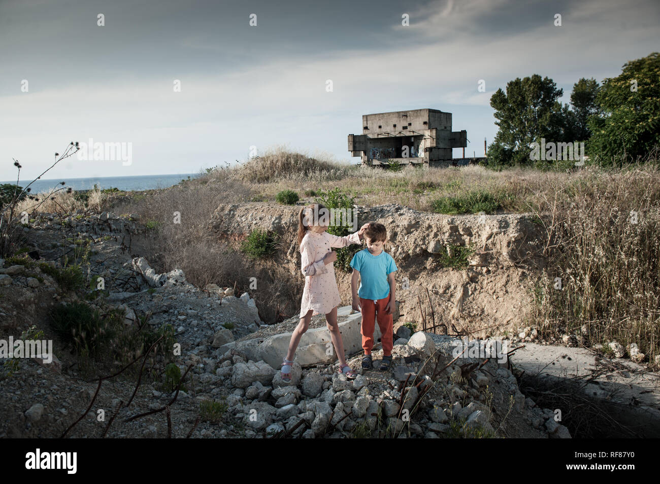 thin little girl refugee soothe her small brother on ruins of ...