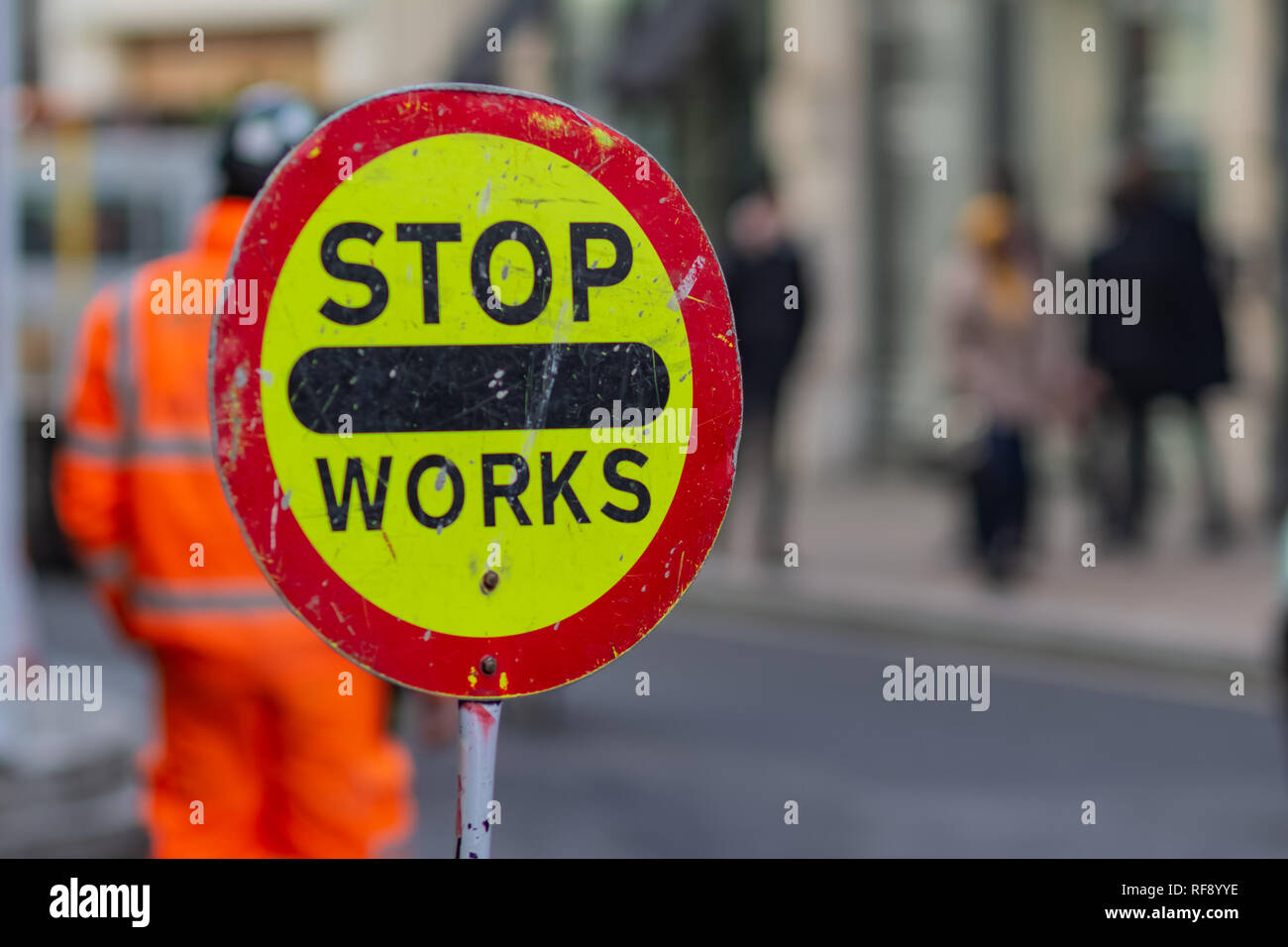 Warning sign Stop Works and a man in orange working in background on ...