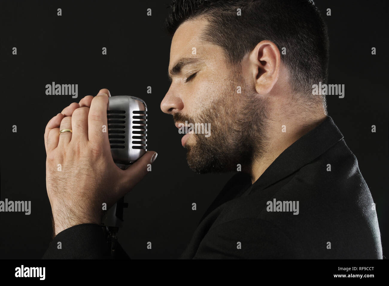 Portrait of male singer with old fashioned microphone against black ...