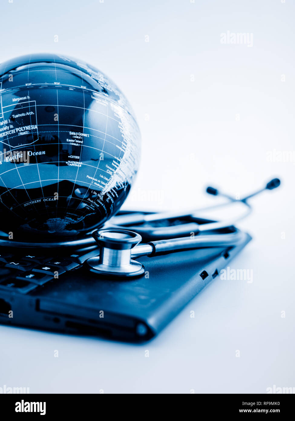 Glass globe and stethoscope on a computer keyboard.blue toned images ...
