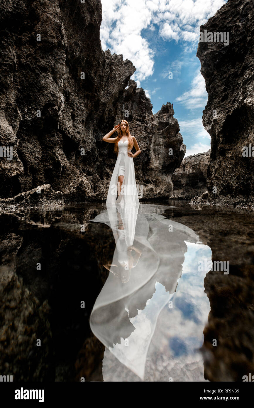 A lovely young girl in a white dress in a sea creek, reflected in the ...