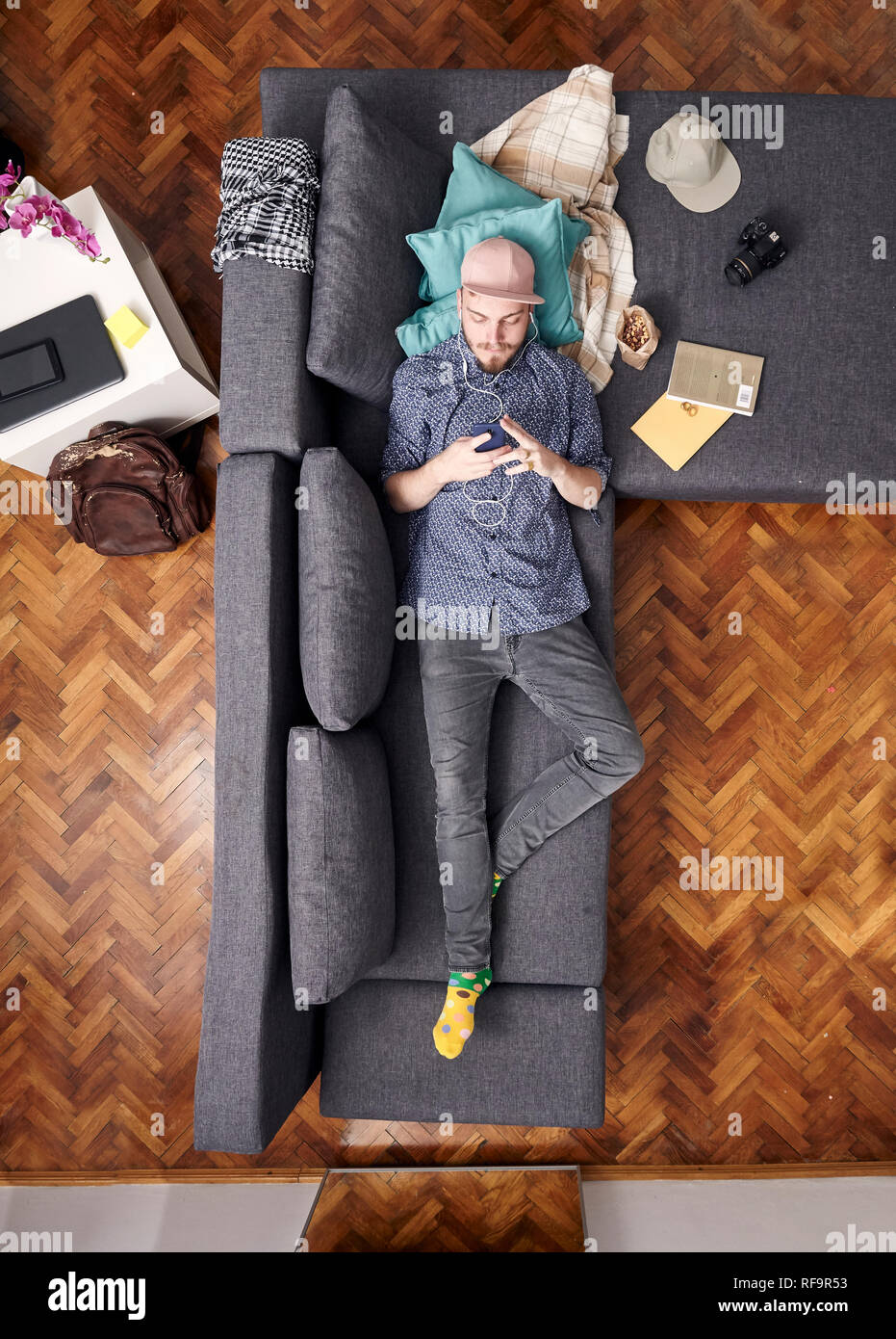 one young hipster, laying in couch in his room. using smartphone. bird ...