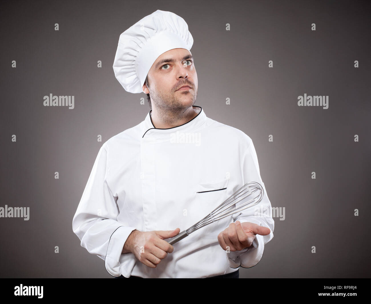 Chef with whick looking up against grey background Stock Photo - Alamy