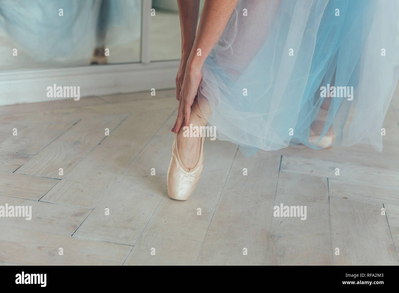 Hands of ballerina in blue tutu skirt puts on pointe shoes on leg in ...