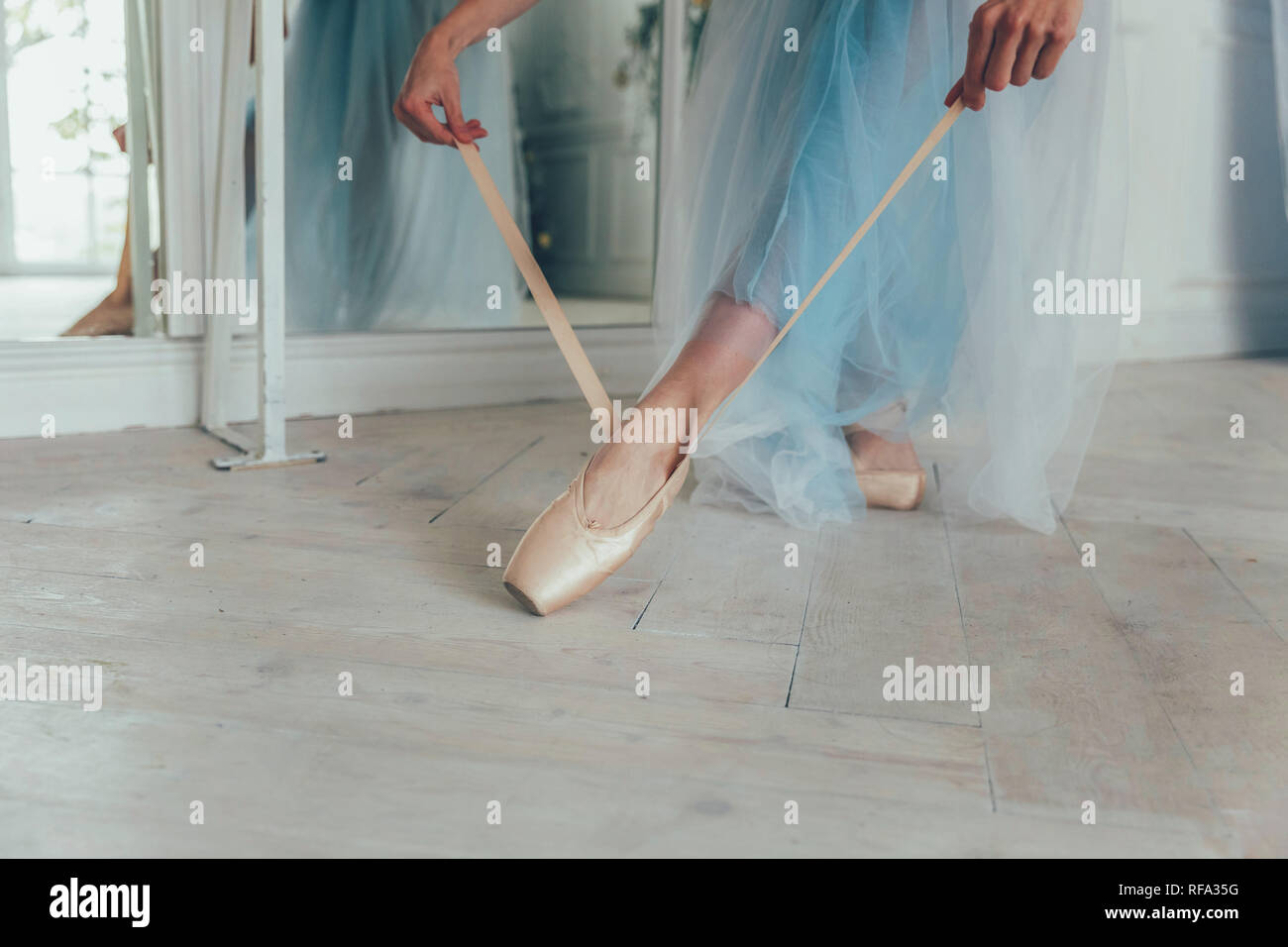 Hands of ballerina in blue tutu skirt puts on pointe shoes on leg in ...