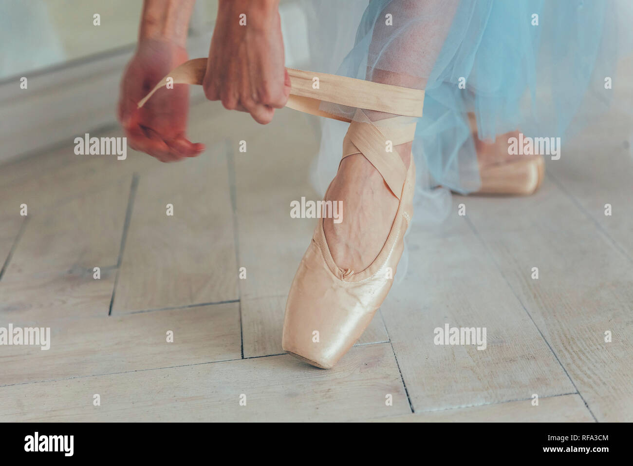 Hands of ballerina in blue tutu skirt puts on pointe shoes on leg in ...