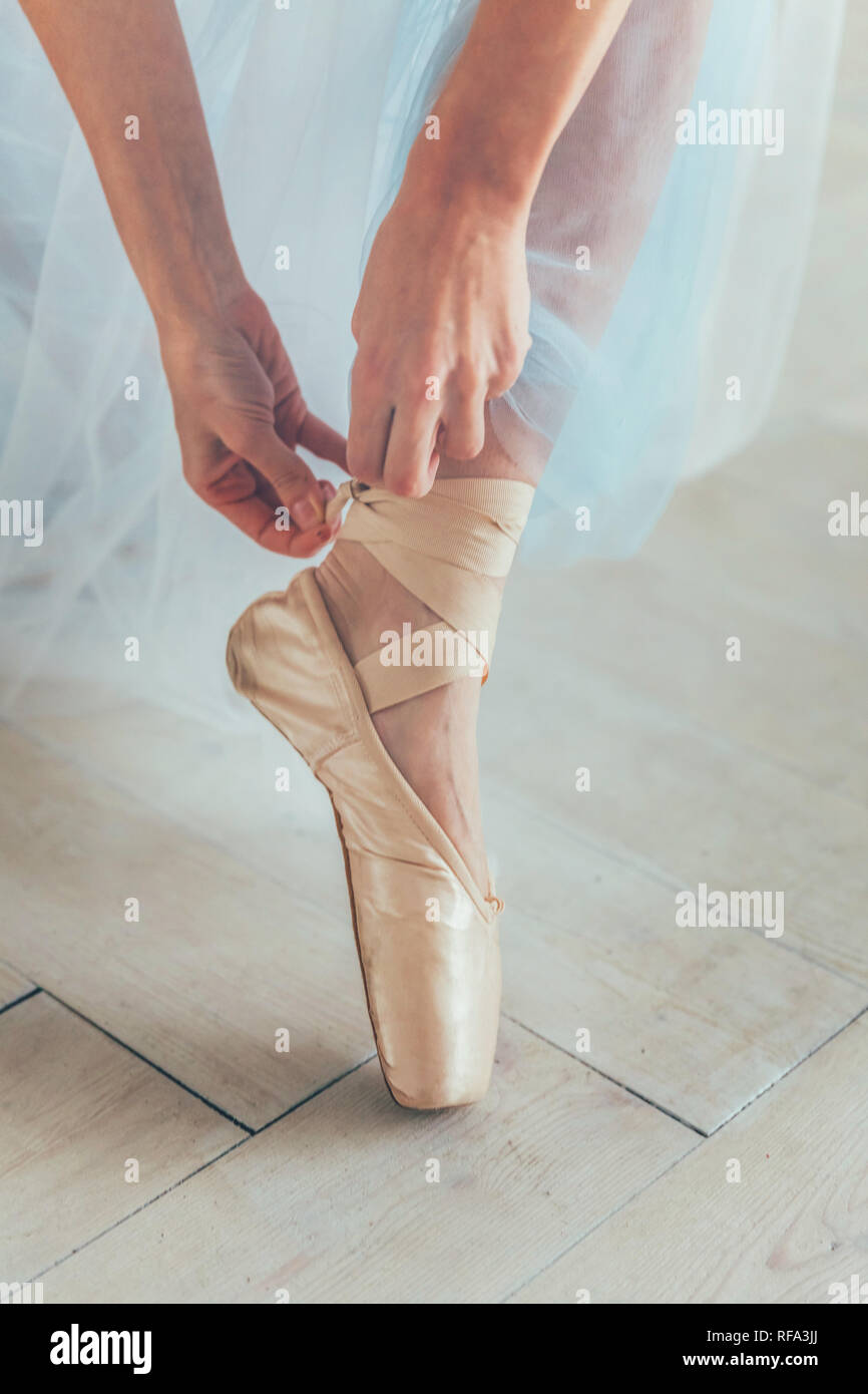 Hands of ballerina in blue tutu skirt puts on pointe shoes on leg in ...