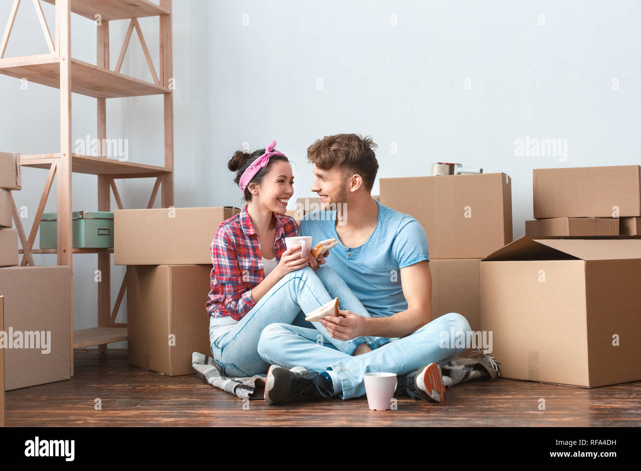Young couple moving to new place sitting eating sandwiches drinking tea ...