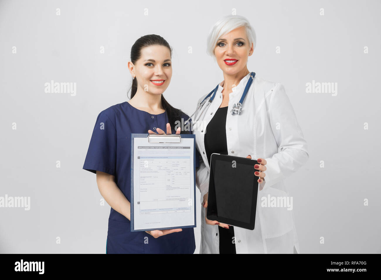 Two female doctors with tablet and sheet with analysis in hands ...