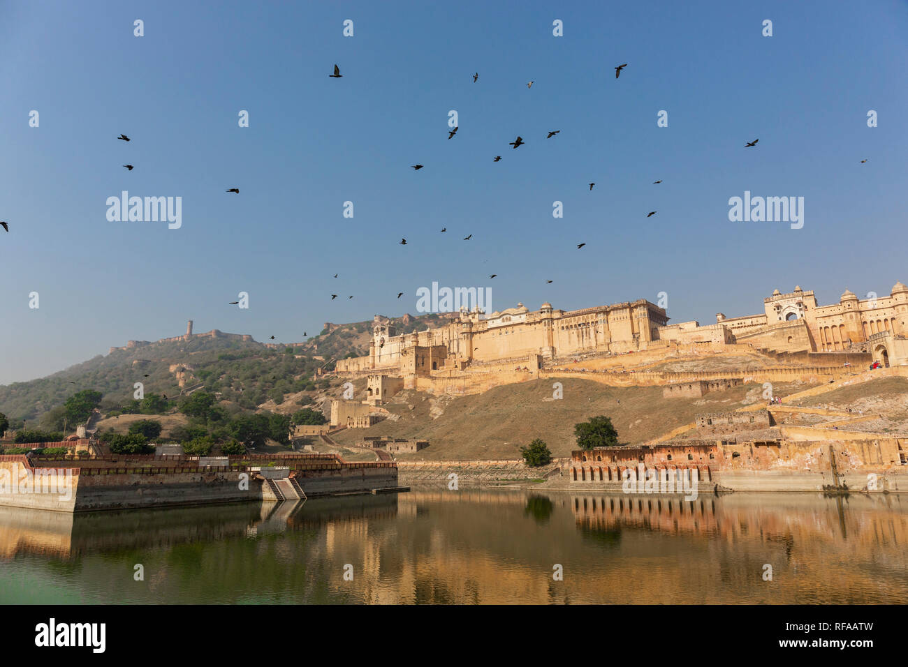 Amber Fort illuminated by warm light of the rising sun and reflected in ...