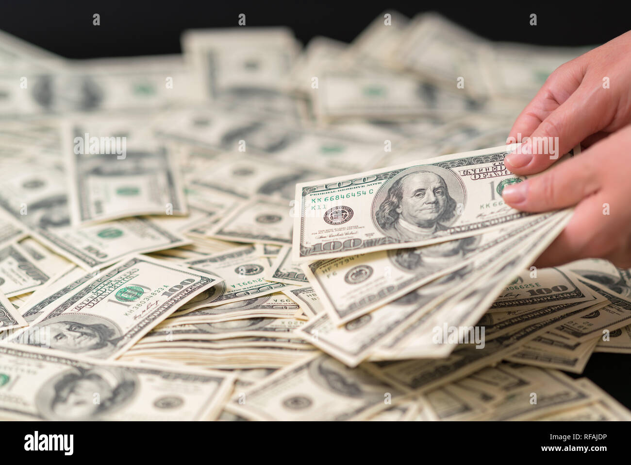 Woman holding a handful of 100 USD banknotes over a table scattered ...