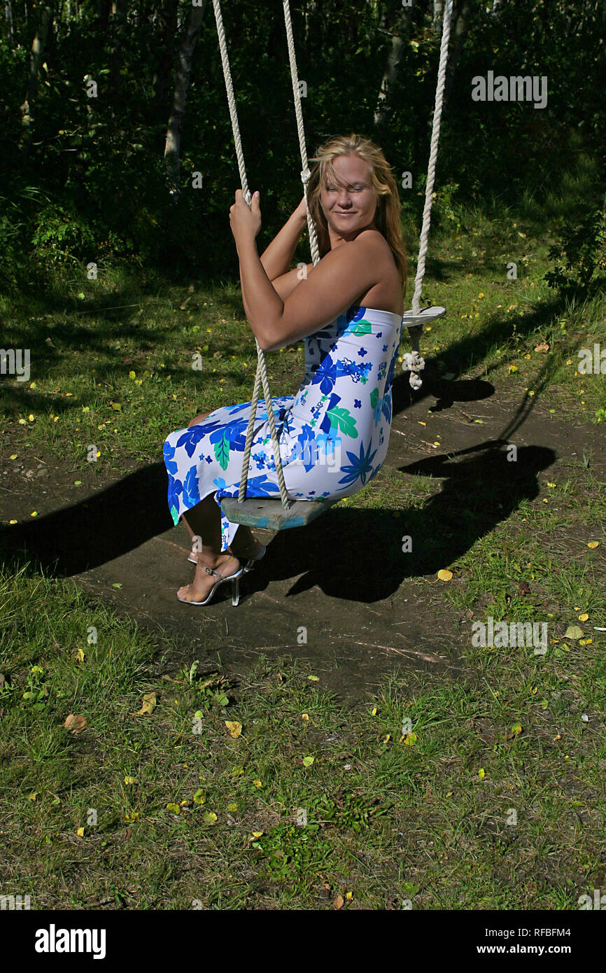 Pretty blonde woman on a swing in a treed area Stock Photo - Alamy