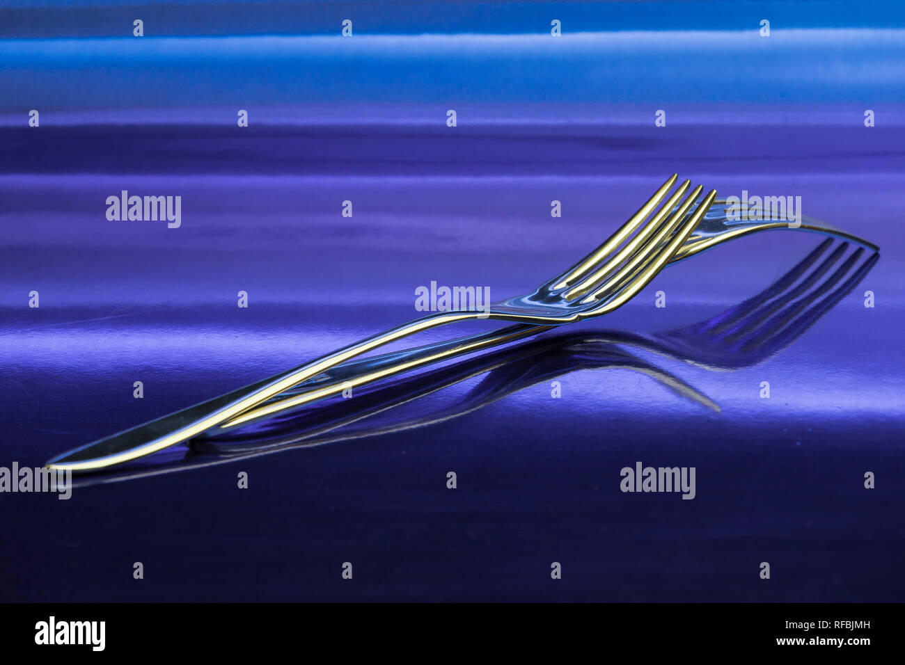 two forks one on top of the other placed on a metallic blue surface ...