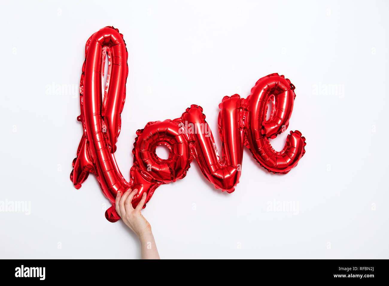 Red foil Love balloon held against a plain white background Stock Photo ...