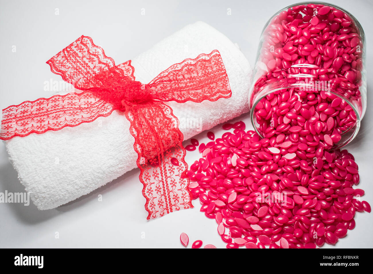 on a white background is a red granular wax in a glass jar and a white ...