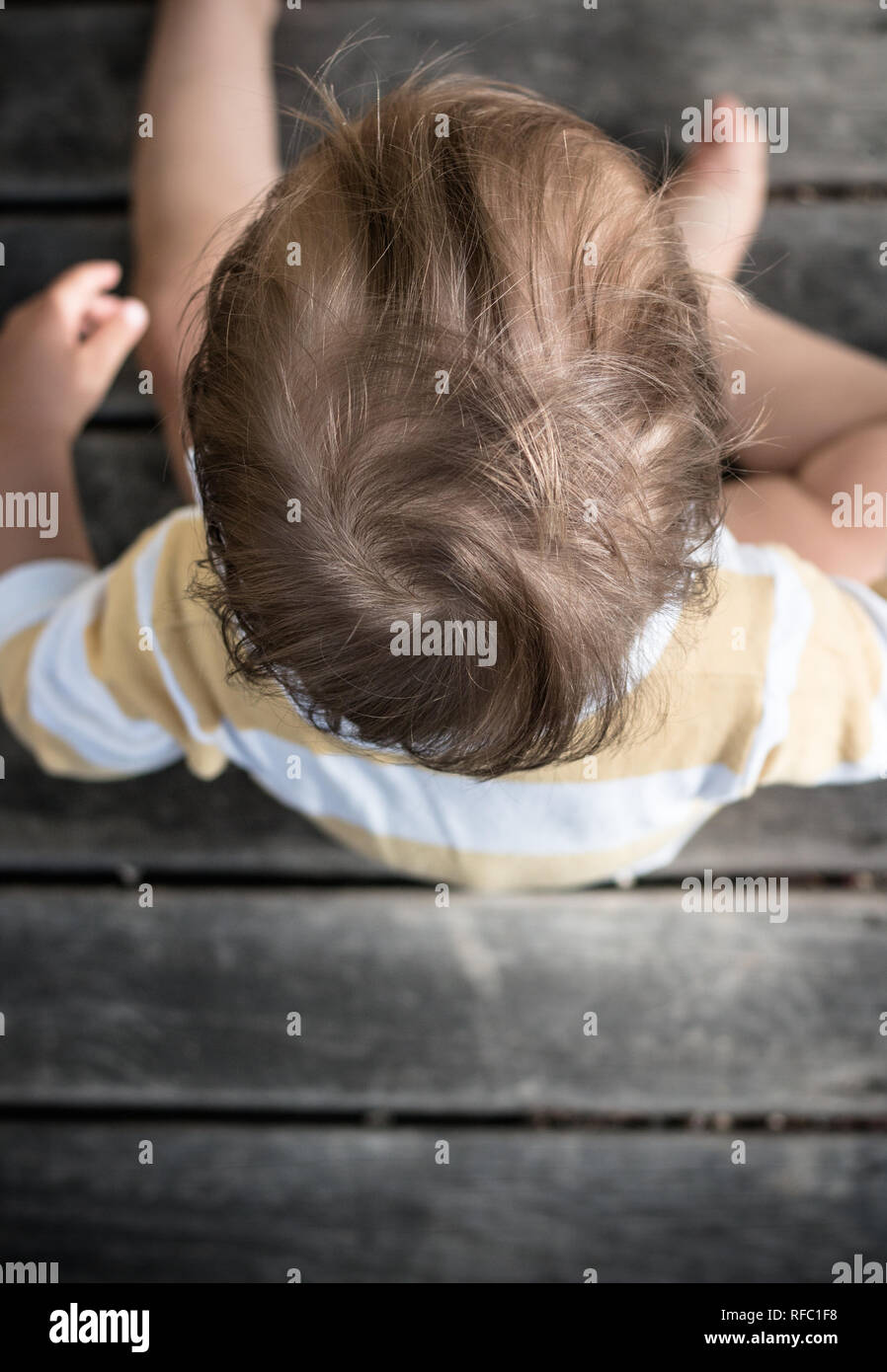 Top down view of toddler boy sitting on the deck on a summer day ...