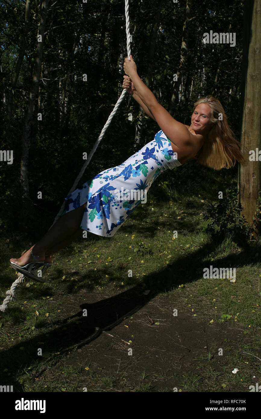 Pretty blonde woman on a swing in a treed area Stock Photo - Alamy