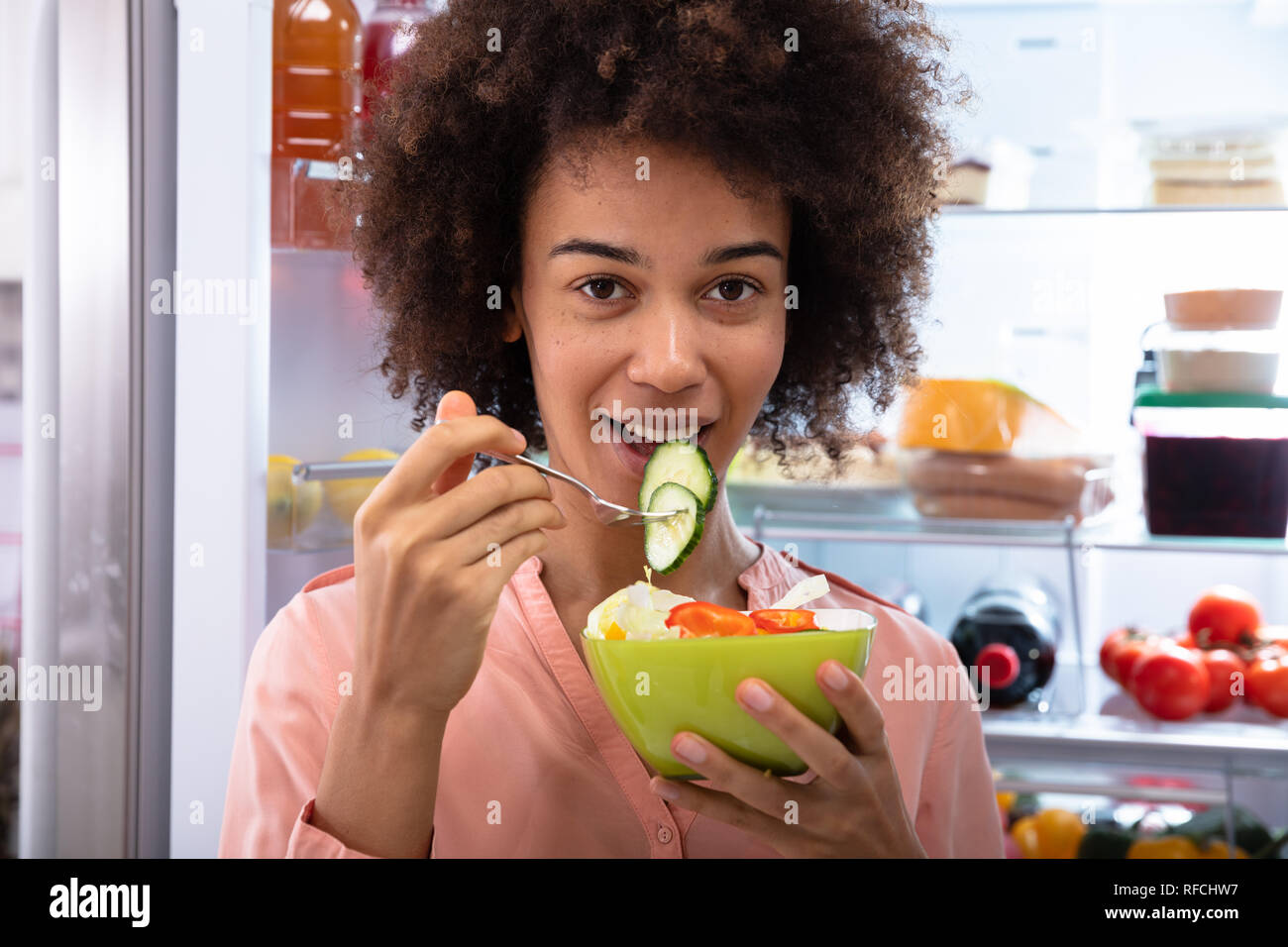Happy Young Woman Standing In Front Of Refrigerator Eating Salad With ...