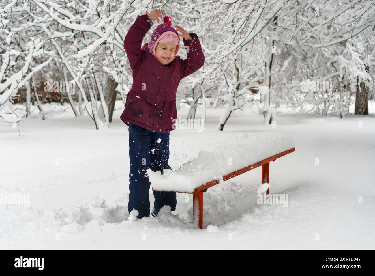 Little cute girl in winter outdoors. She throws snow up. Girl rejoices ...