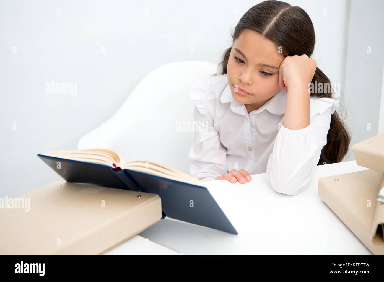 Reading boring book. Girl child reads book while sit table white ...