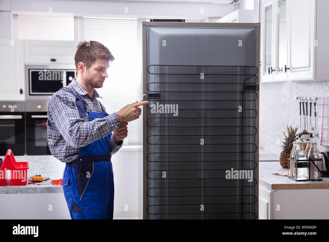 Serviceman In Overall Working On Fridge With Wrench In Kitchen Stock ...