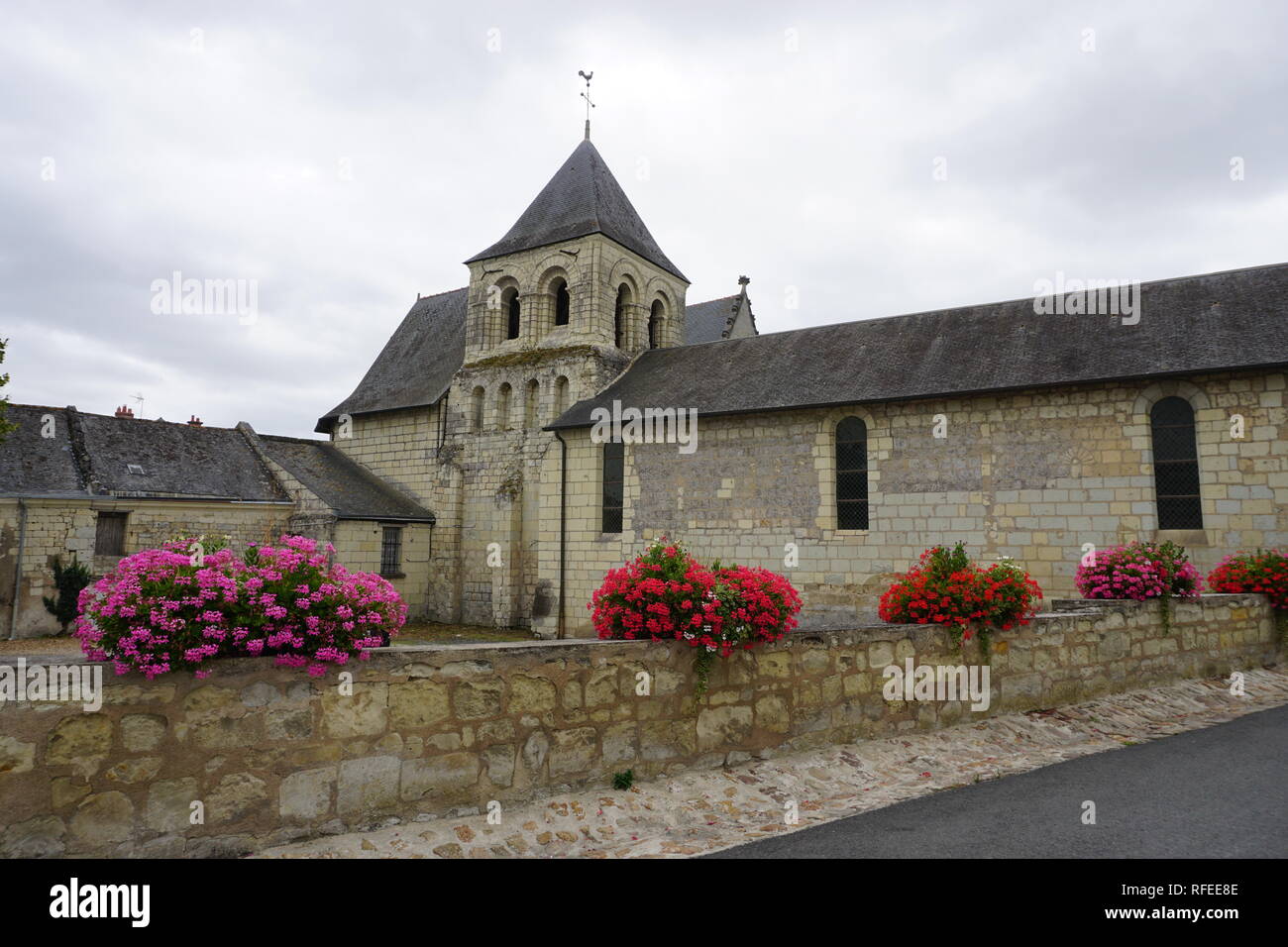 Old limestone church and outside wall with bright colorful flowers pots ...