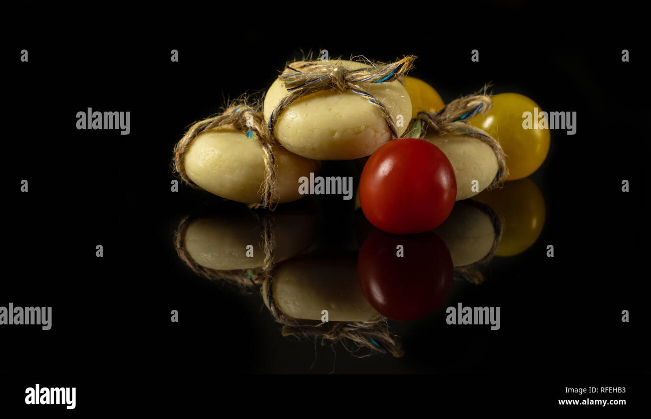 Small round cheeses with red and yellow tomatoes on a dark background ...