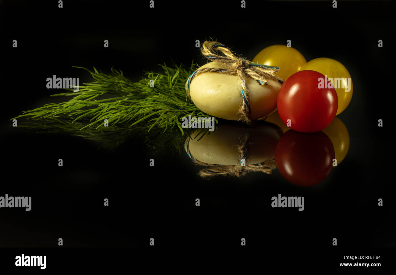 Small round cheese head with vegetables and greens on dark background ...