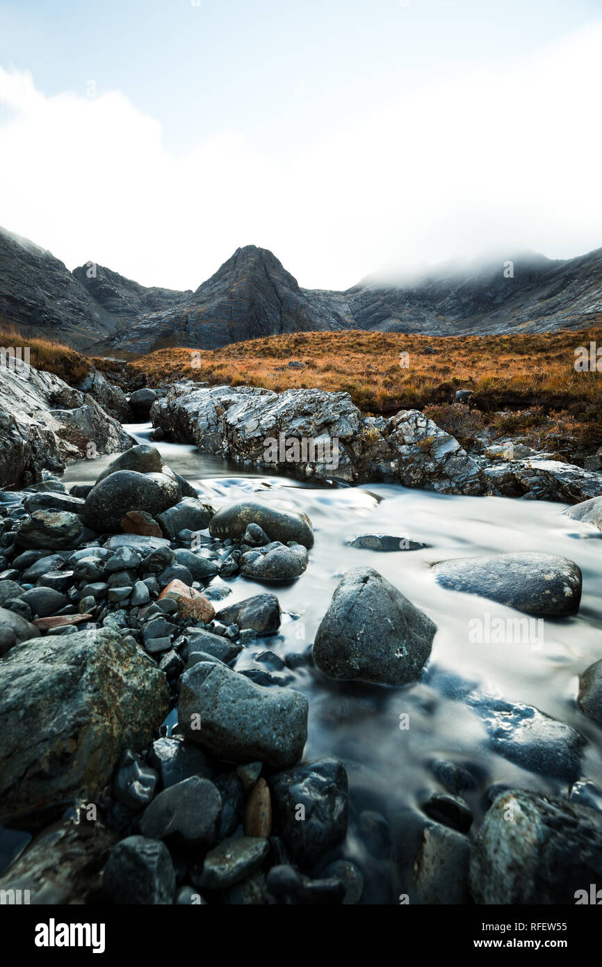 Long exposure of river stream with colourful stones in front of fog ...