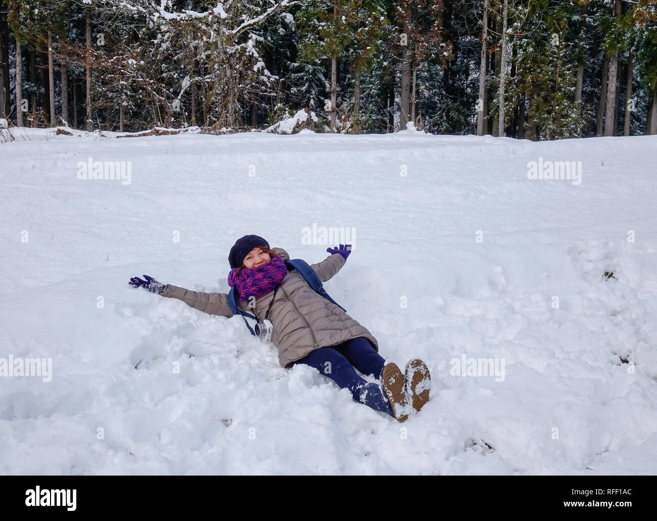Happy woman lying on snow with green forest background Stock Photo - Alamy
